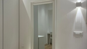 Quarto com um espelho grande, um guarda-roupa, uma mesa de cabeceira e um candeeiro fixado na parede.