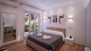 Quarto moderno com cama grande, escrivaninha e varanda com vista para árvores.