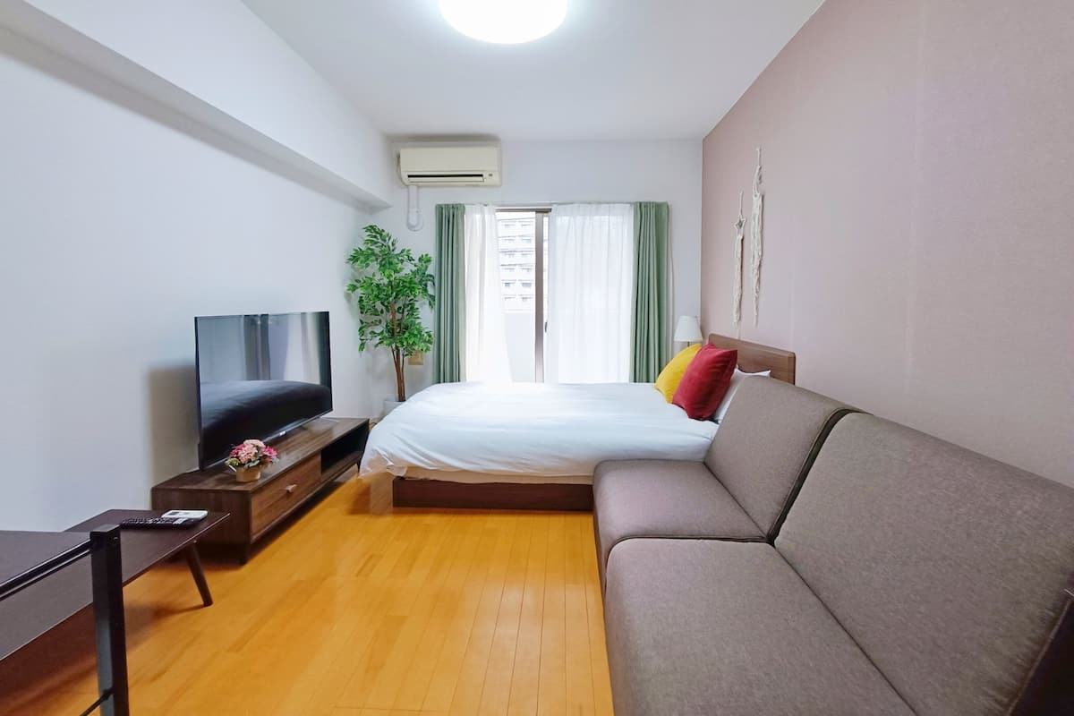 Quarto de hotel moderno com cama, sofá, televisão e piso de madeira.