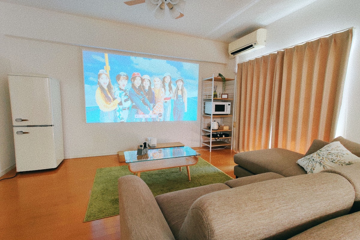 Sala de estar com televisão de tela plana, ventilador de teto, micro-ondas e geladeira.