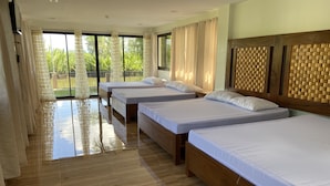 Quarto de hotel com três camas de madeira, uma grande porta de correr de vidro que dá para uma varanda e cabeceira de cama trançada.