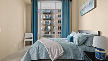 Quarto com cama, cadeira, mesa de cabeceira e janela com cortinas.