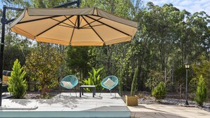 Uma área na piscina com um espaço de estar coberto, duas cadeiras, uma mesa e um poste de luz.