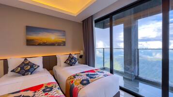 Quarto de hotel com duas camas, uma janela grande com vista para a cidade, um quadro na parede e uma luminária no teto.