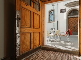 Uma porta de madeira com puxador de metal, chão de azulejos com padrão floral e uma placa na parede com a inscrição "Mennigasse".