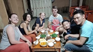Um grupo de pessoas sentadas em torno de uma mesa de madeira com vários pratos, em um ambiente rústico e simples.
