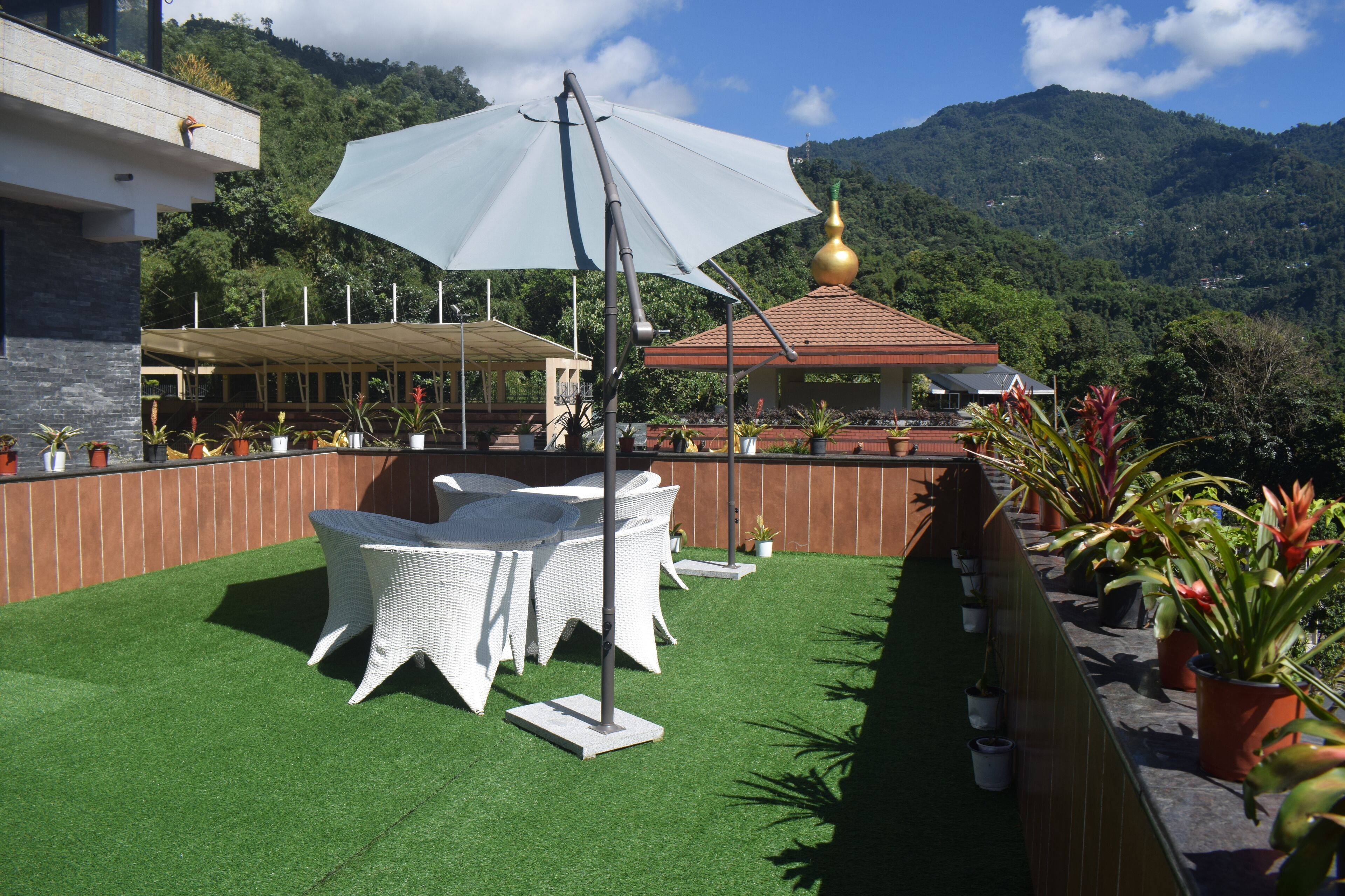Terraço no telhado com grama sintética, móveis de vime branco e um guarda-sol grande.