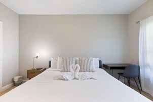 Quarto de hotel com cama arrumada, uma escrivaninha, uma cadeira e uma luminária.