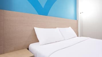 Cama bem arrumada com lençóis e almofadas brancos, cabeceira de madeira e uma pequena mesa de cabeceira.