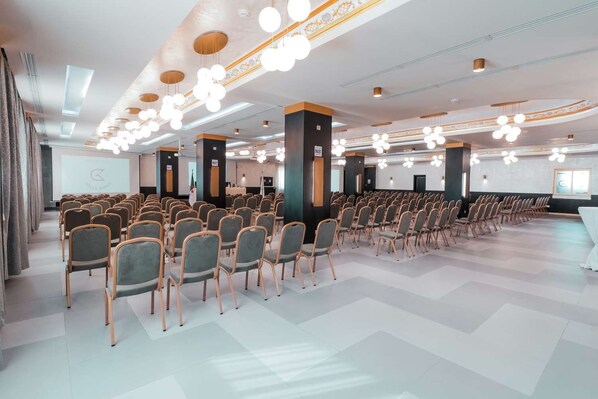 Uma sala de conferências com fileiras de cadeiras, uma tela de projeção e um palco.