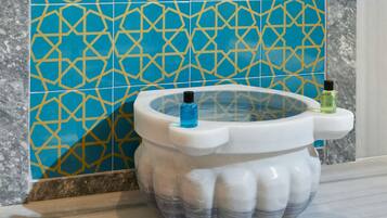 Um banheiro com parede de azulejos estampada em azul e dourado, pia de mármore branco e toalha vermelha e branca.
