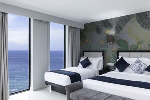 Quarto de hotel com duas camas, vista para o oceano e decoração temática tropical.