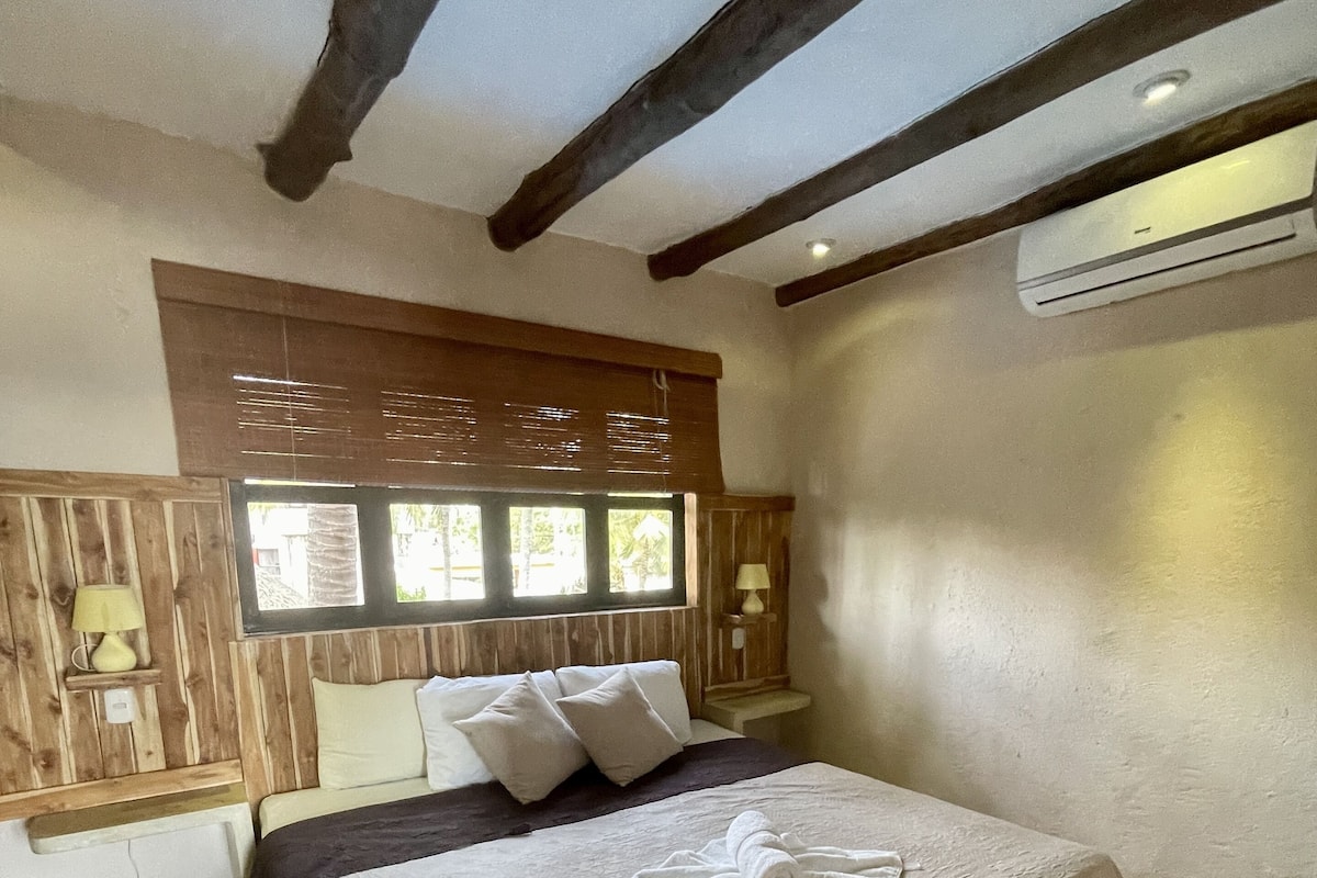 Quarto com cama, janela, luminária e ar-condicionado fixado na parede.
