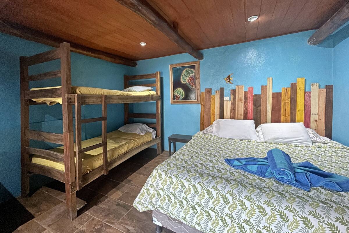 Um quarto com beliches, uma cama com colcha estampada, cabeceira de madeira e um quadro na parede.