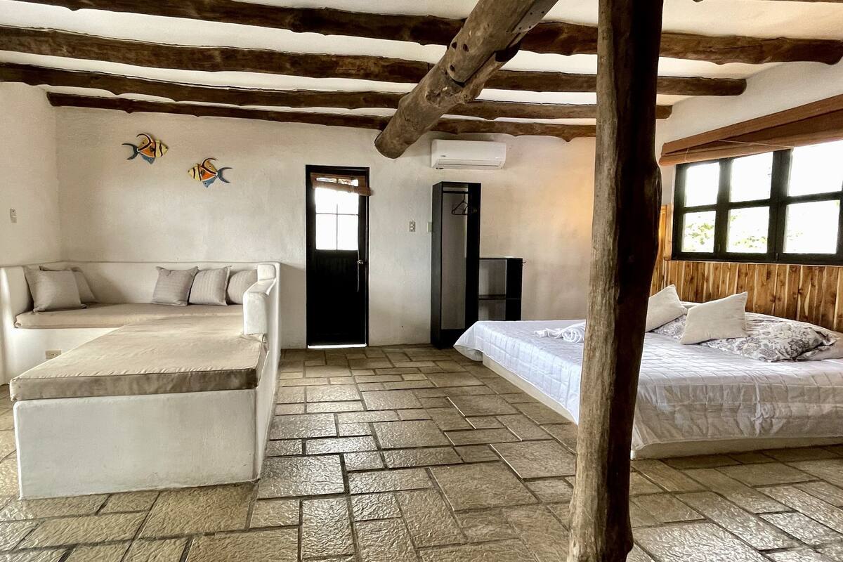 Um quarto com sofá, cama, teto de madeira, chão de azulejos e uma porta.