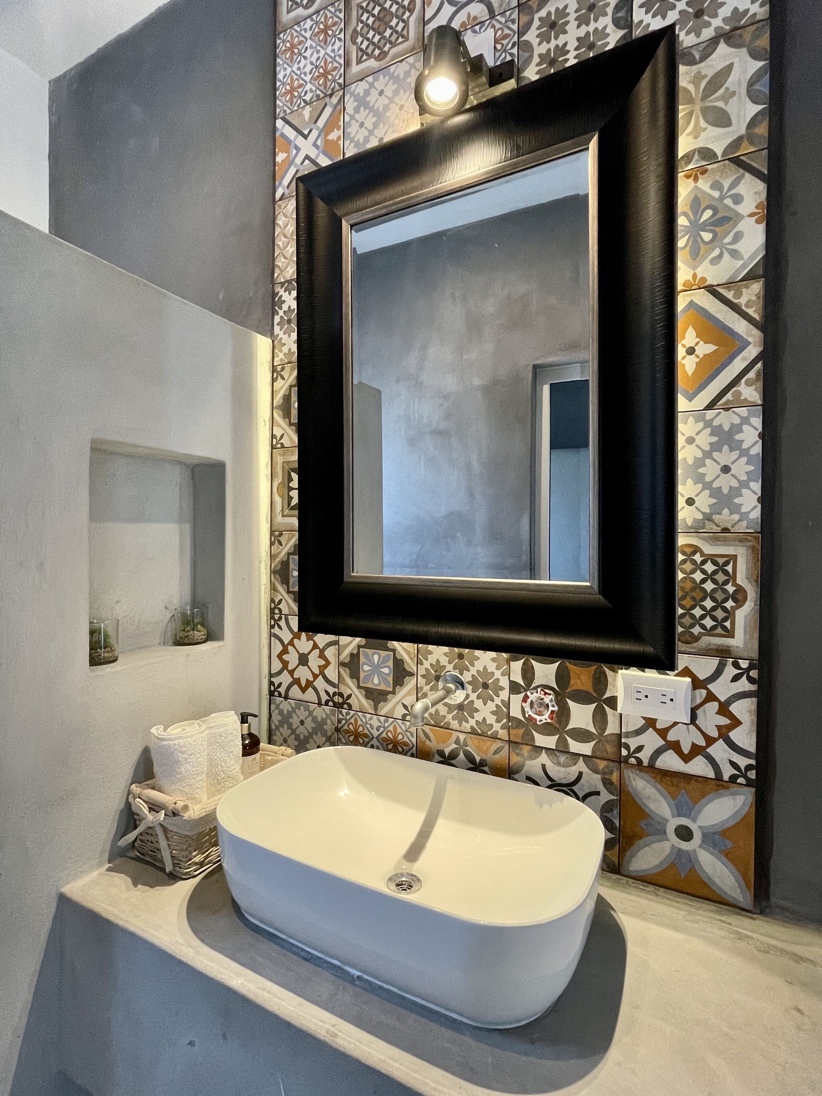Casa de banho com lavatório branco, espelho e painel de azulejos.