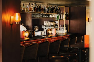 Uma área de bar com várias prateleiras de garrafas, um balcão e algumas cadeiras.