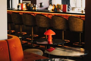Uma área de bar com mesas redondas, assentos acolchoados e um abajur vermelho.