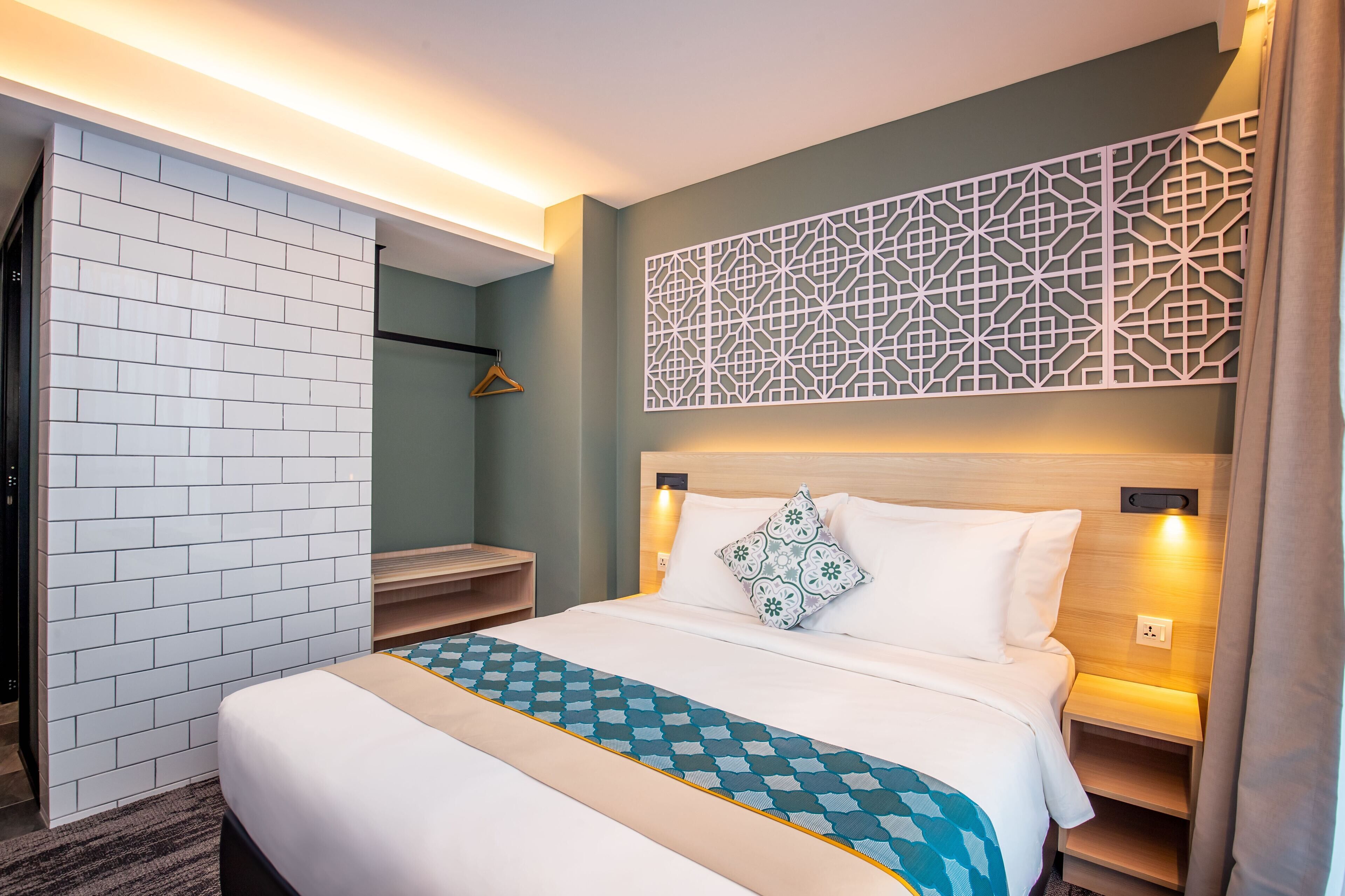 Quarto de hotel moderno com uma cama bem arrumada, um painel decorativo fixado na parede e uma mesa de cabeceira com luminária.