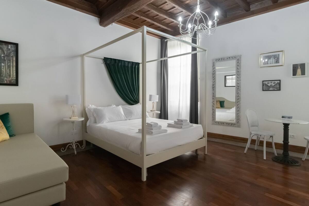 Um quarto com uma cama de dossel, um sofá, uma mesa pequena, uma cadeira e um lustre.