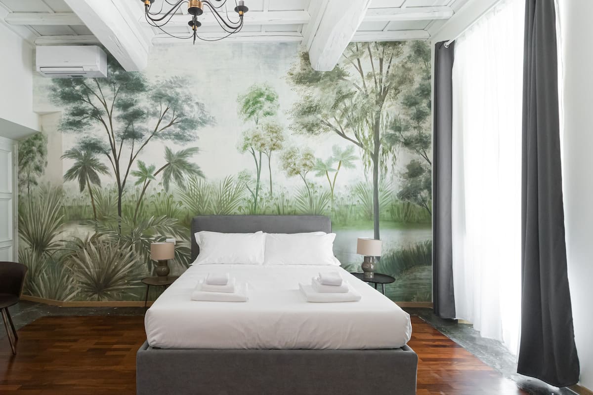 Quarto com cama, mesas de cabeceira, uma cadeira e um mural com uma cena de floresta.