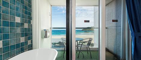 Casa de banho com banheira e vista para a praia através de uma porta de vidro.