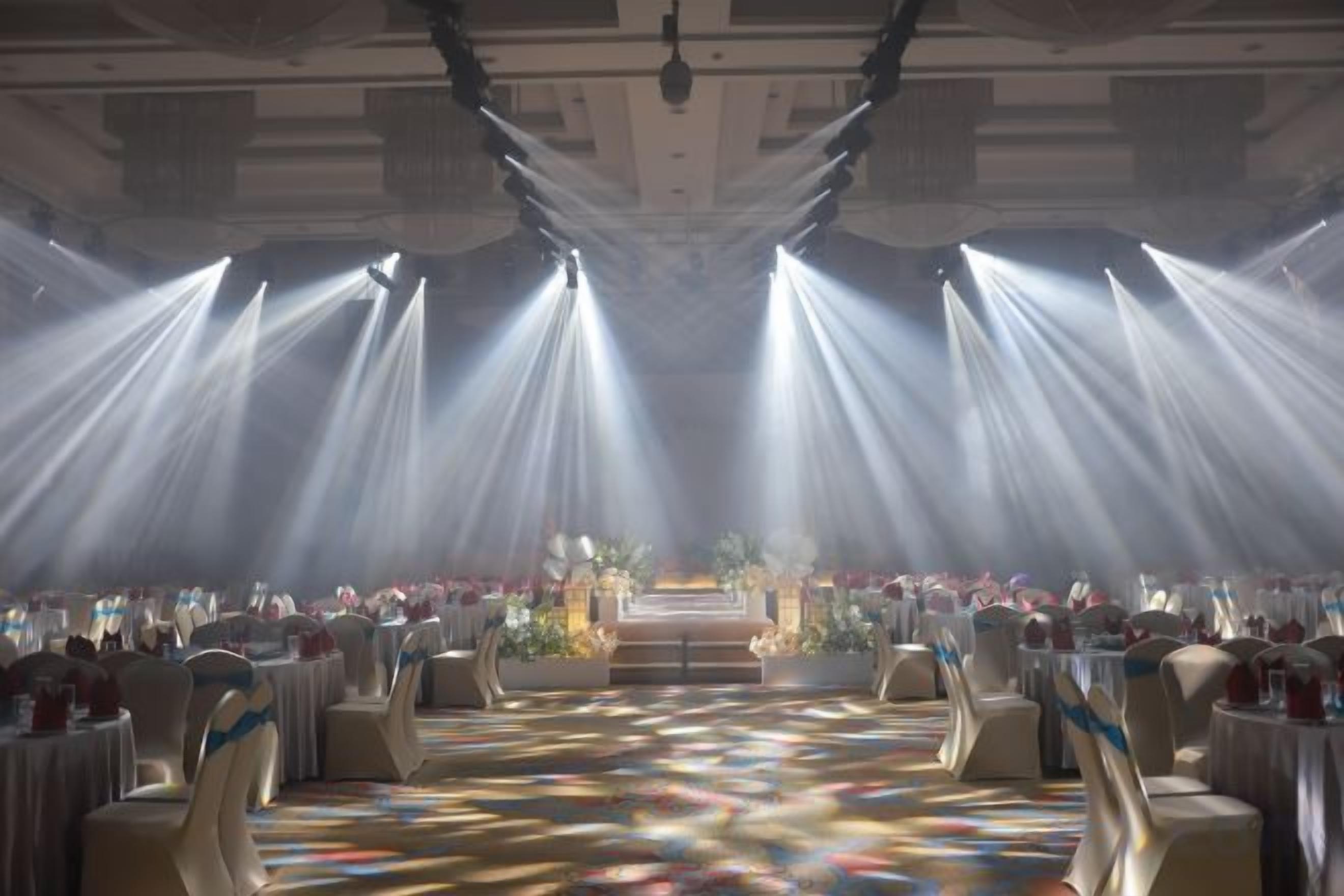 Uma sala de banquetes com fileiras de mesas e cadeiras, um palco central e piso estampado.