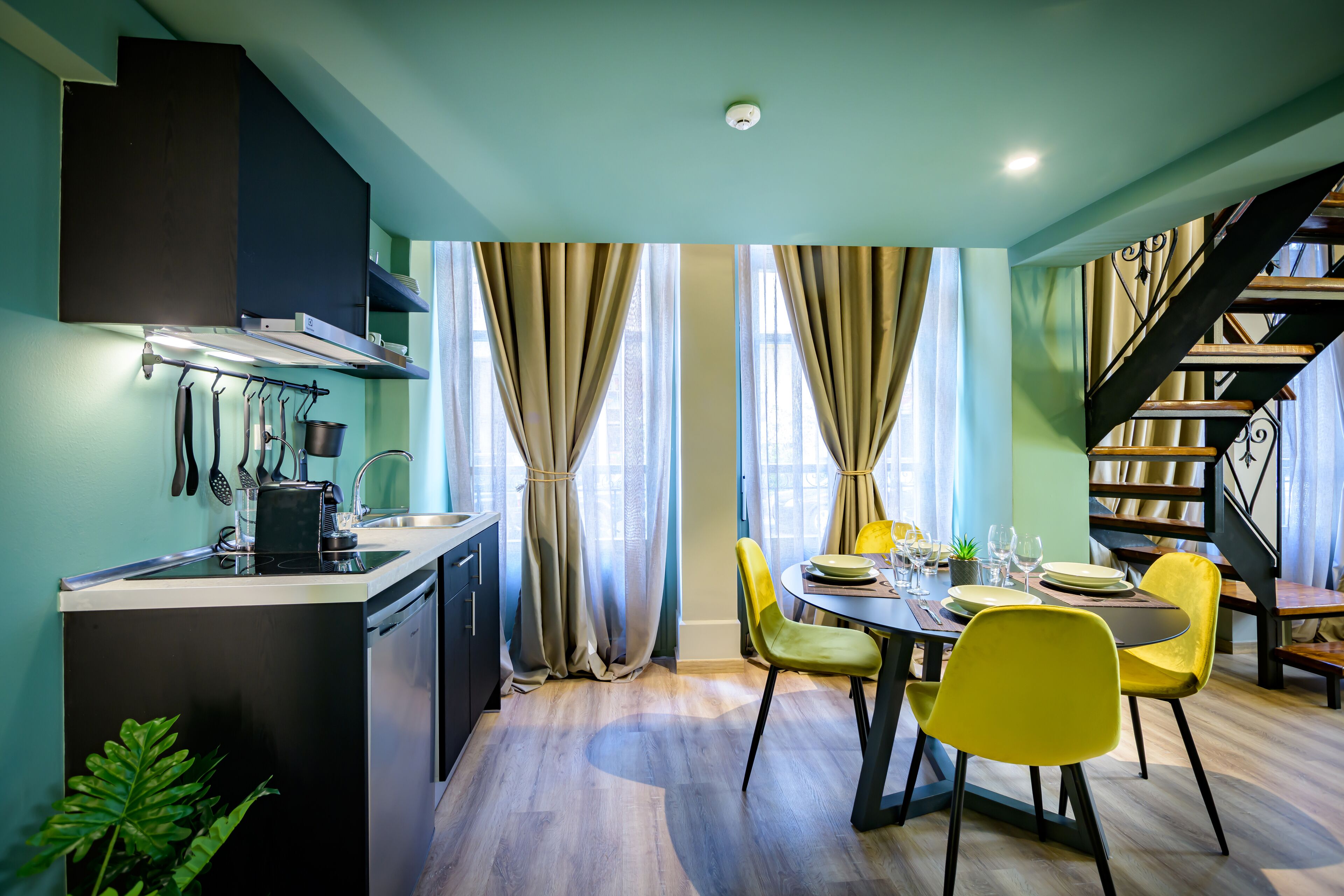 Uma cozinha moderna com área de jantar, incluindo uma escadaria, uma mesa de jantar com cadeiras e vista para a cidade através de grandes janelas.