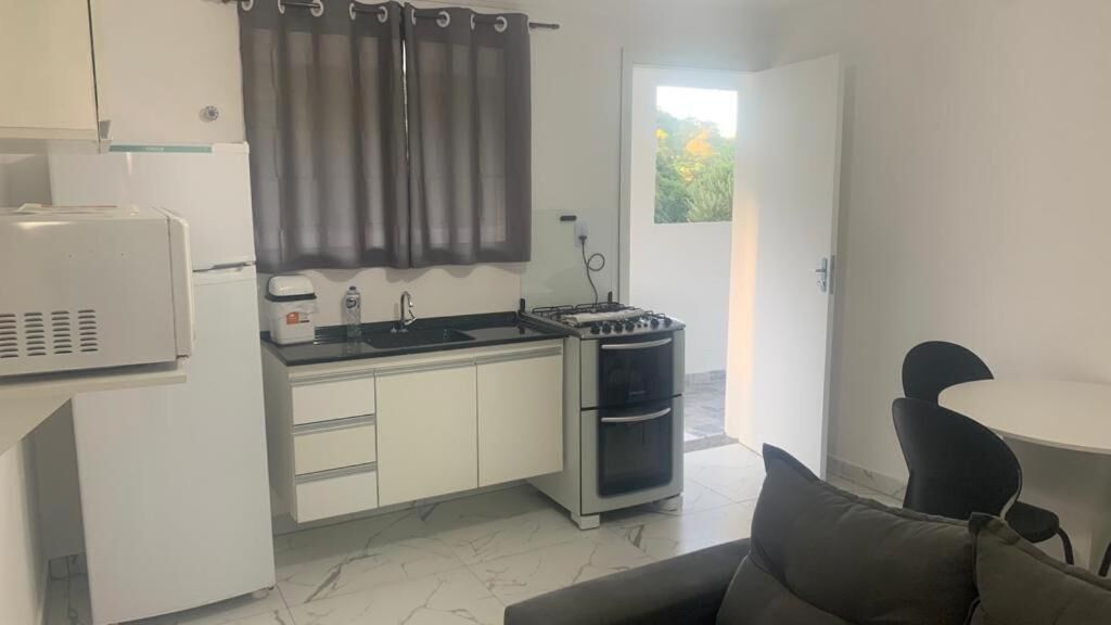 Uma cozinha compacta com geladeira, fogão, pia e uma área de refeições com mesa e cadeiras.