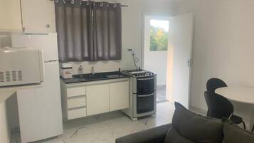 Uma cozinha compacta com geladeira, fogão, pia e uma área de refeições com mesa e cadeiras.
