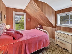 Quarto com cama, penteadeira, janela e porta para uma varanda.