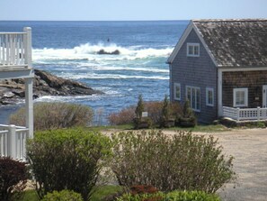 Uma casa à beira-mar com varanda, costa rochosa e ondas quebrando.