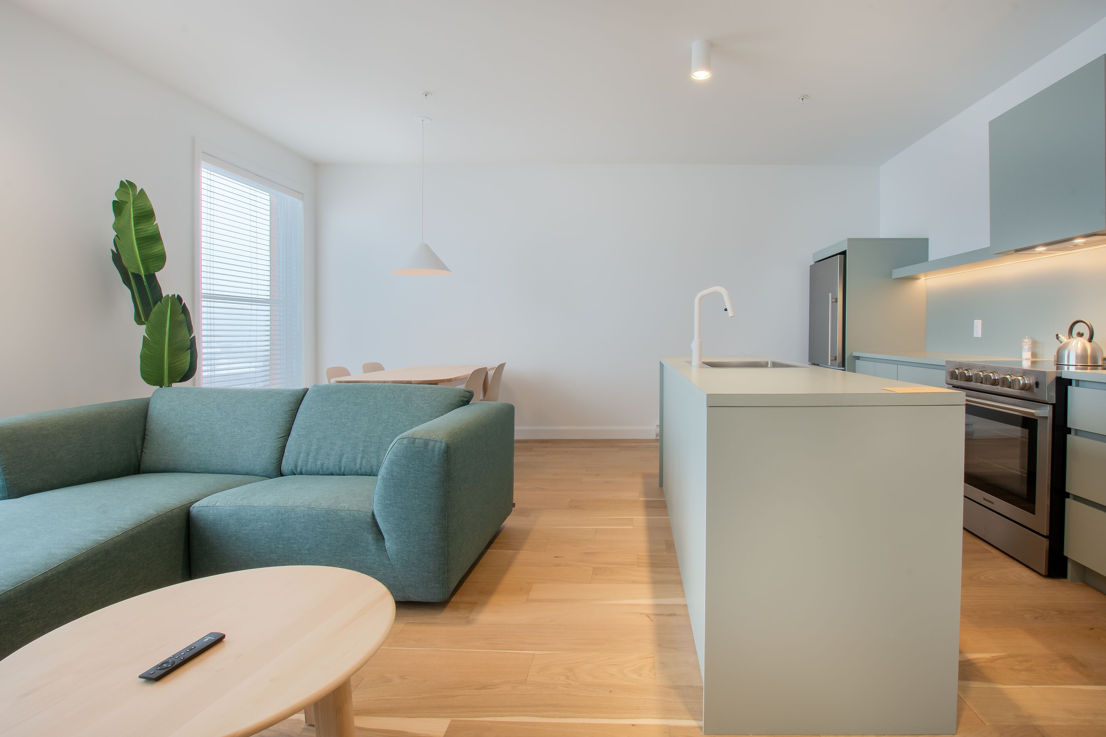 Um espaço de estar moderno com sofá, mesa de centro e área de cozinha equipada com frigorífico e forno.