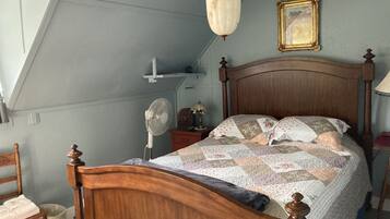 Quarto com cama de madeira, ventilador de teto, abajur e quadro pendurado na parede.