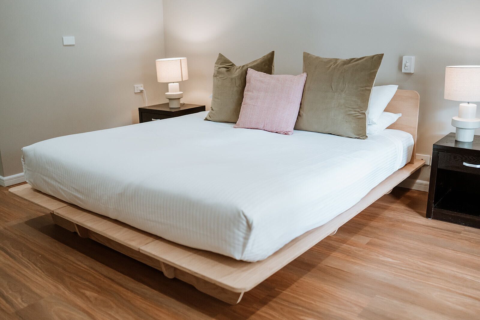 Quarto moderno com cama em plataforma de madeira, duas mesas de cabeceira com luminárias e esquema de cores neutras.