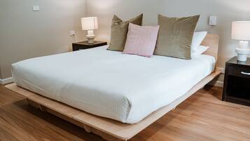 Quarto moderno com cama em plataforma de madeira, duas mesas de cabeceira com luminárias e esquema de cores neutras.