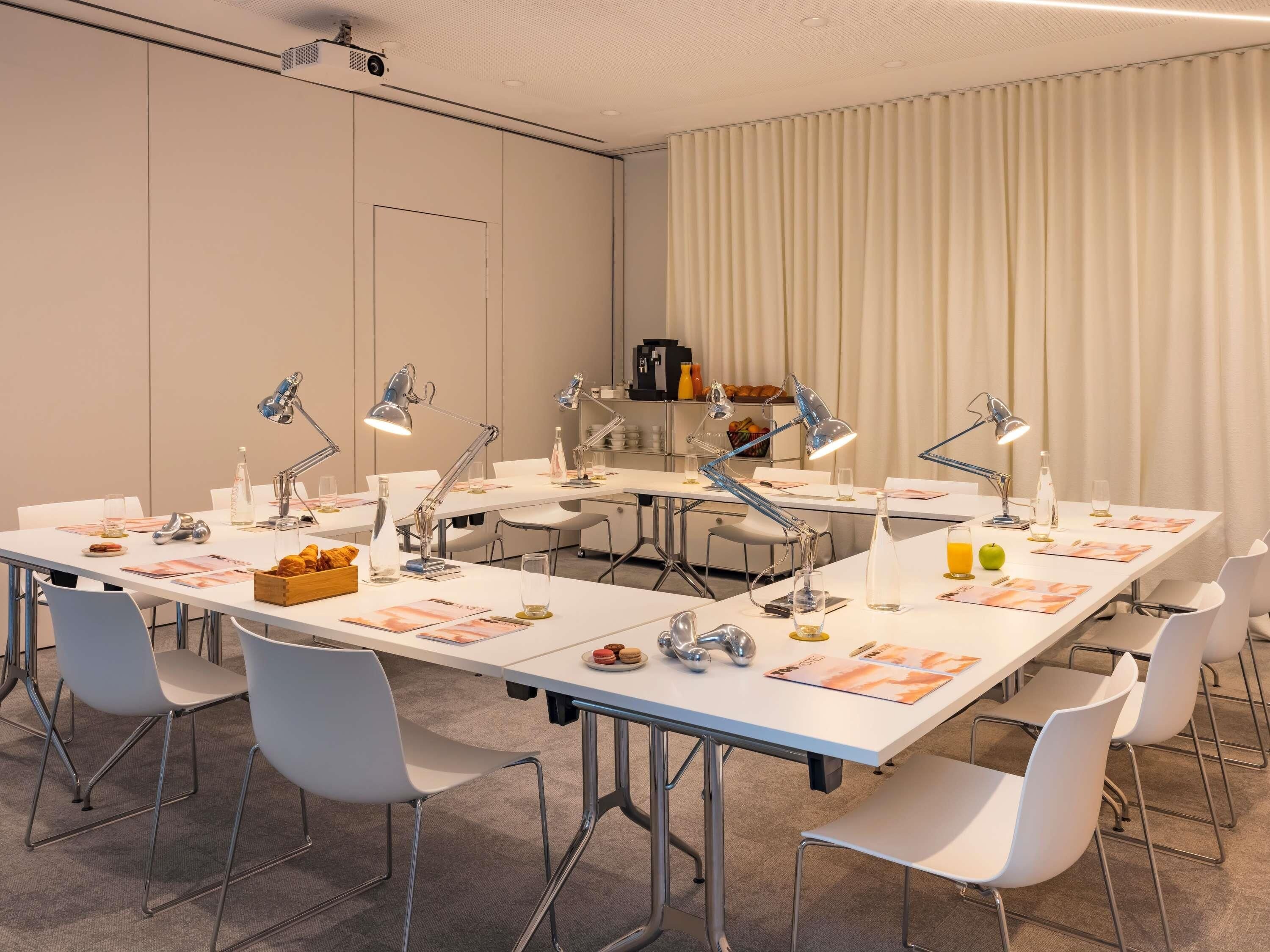 Uma sala de conferências com mesas brancas, cadeiras e várias luminárias de mesa.