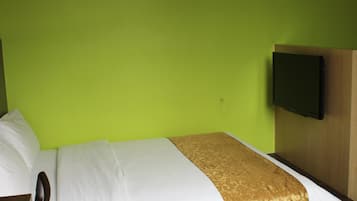 Quarto de hotel com uma cama, uma televisão na parede e uma parede verde.