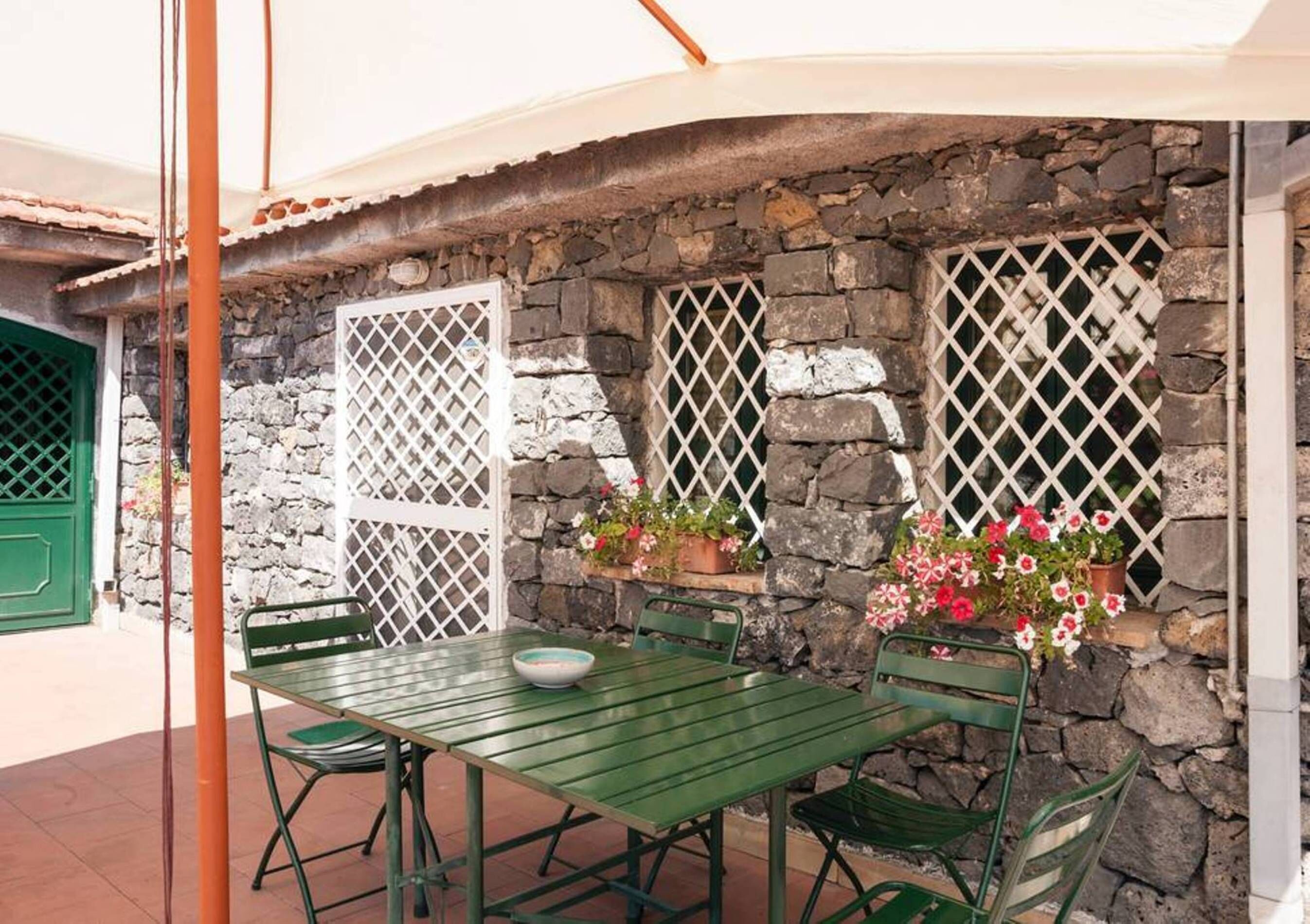 Um pátio com mesa, cadeiras, paredes de pedra e janelas com treliça.