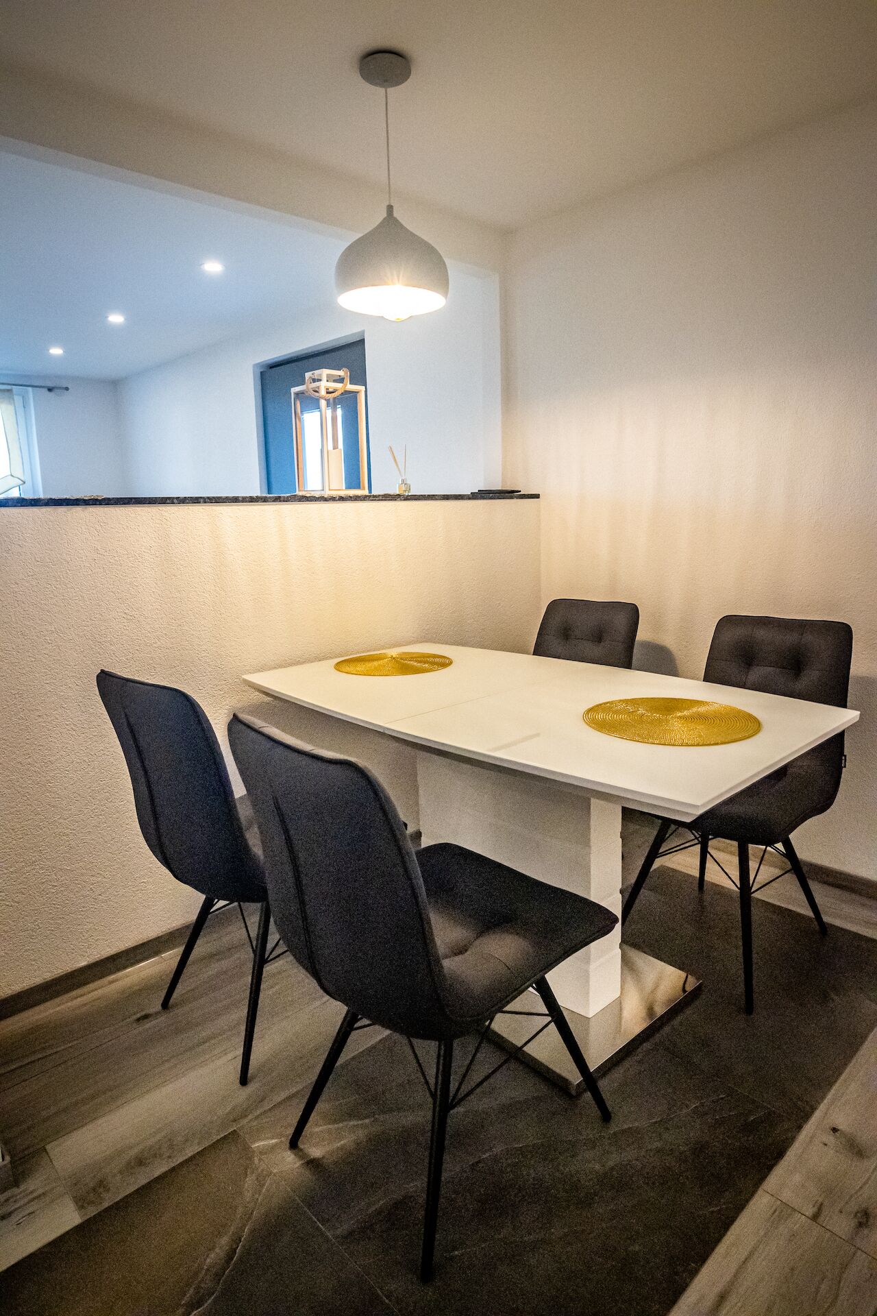 Uma área de refeições moderna com uma mesa branca, cadeiras pretas e uma luminária pendente.