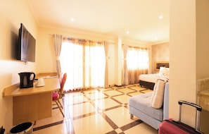 Quarto de hotel com cama, escrivaninha, cadeira, televisão e mala.