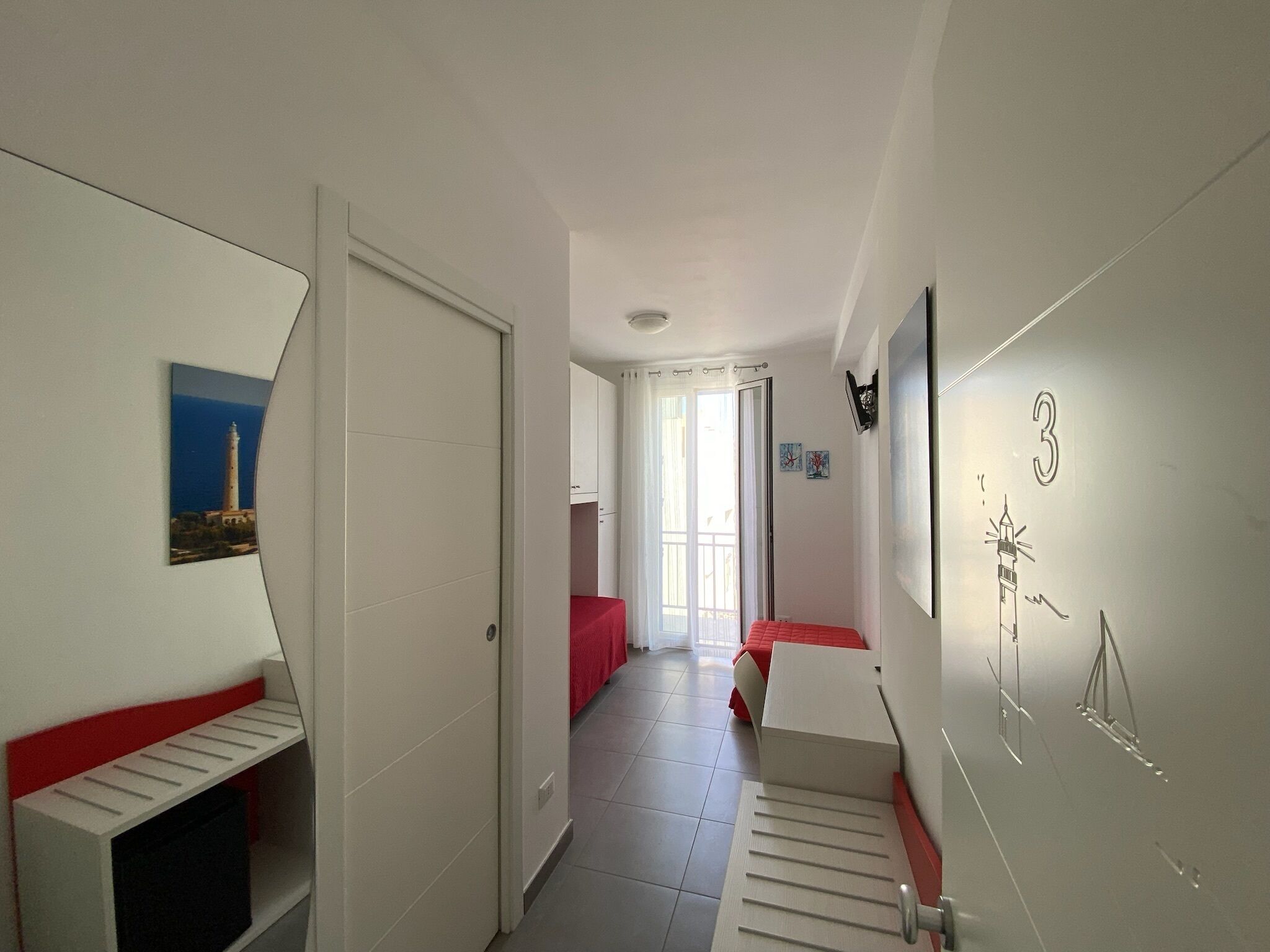 Corredor com uma cama, uma porta, um janelo e uma parede com um número.