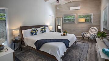 Quarto com cama grande, ventoinha no teto, mesa de cabeceira com abajur, cadeira e janela com persianas.