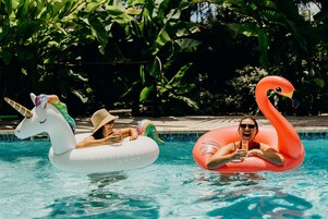 Duas pessoas em uma piscina, cada uma em um flutuador com o formato de um unicórnio e um flamingo.
