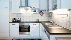 Uma cozinha moderna com armários brancos, forno embutido, micro-ondas e coifa de aço inoxidável.