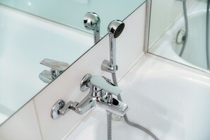 Chuveiro e torneira cromados em um banheiro com box de vidro.