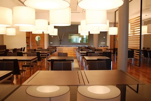 Um restaurante moderno com várias mesas e cadeiras, luminárias pendentes grandes e decoração em madeira.