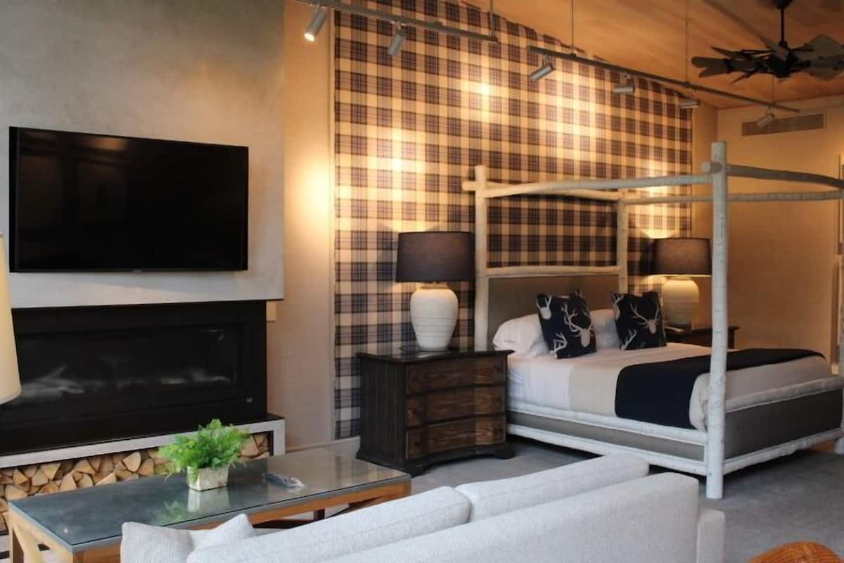 Quarto com cama de dossel, TV de tela plana, lareira, cortina estampada de xadrez e ventilador de teto.