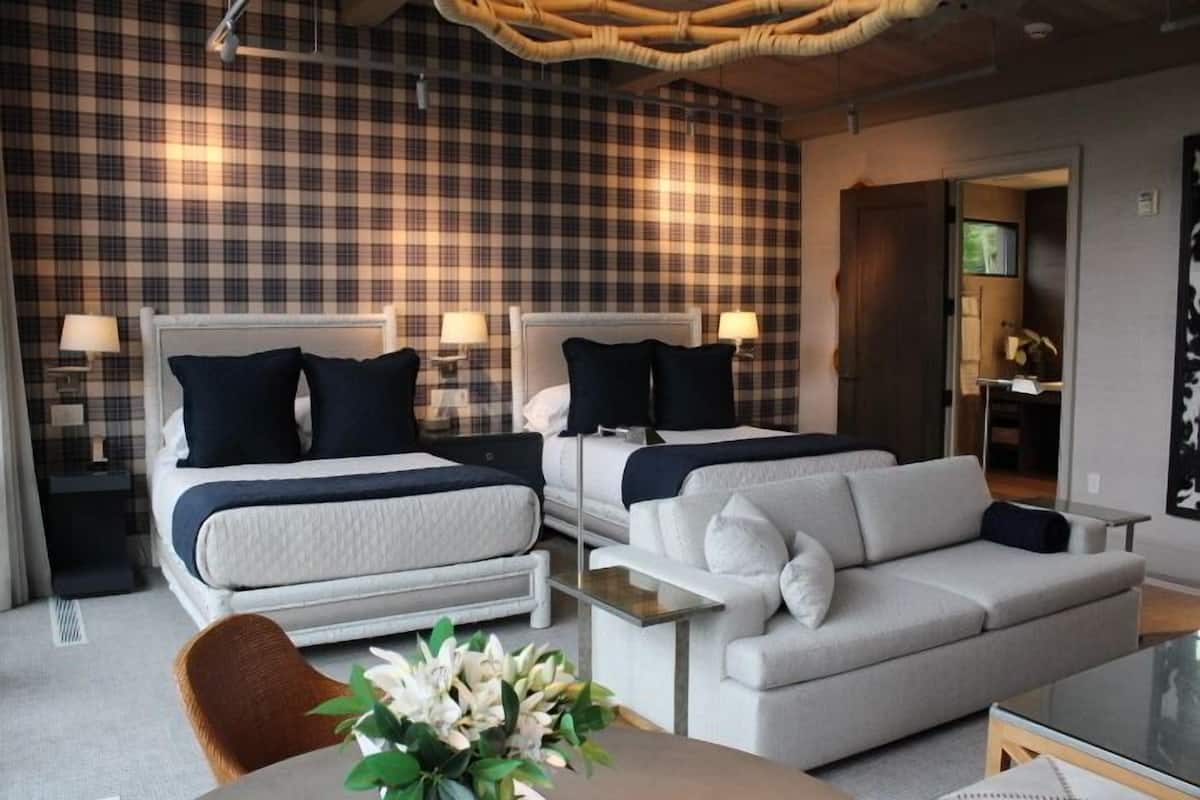 Quarto de hotel com duas camas, um sofá, uma mesinha e uma cadeira.