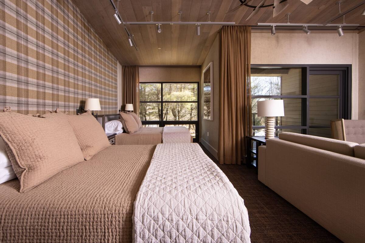 Quarto de hotel com uma cama grande, dois sofás, uma mesa pequena e uma janela com cortinas.